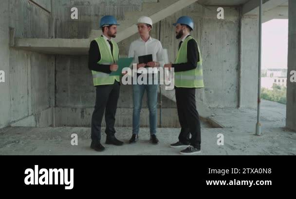 Three young expert engineers analyzing the map of new building using a tablet, wearing a safety ...
