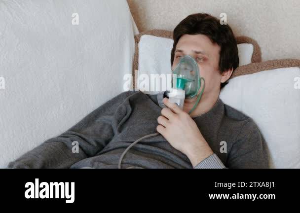 Use nebulizer and inhaler for the treatment. Young man inhaling through ...