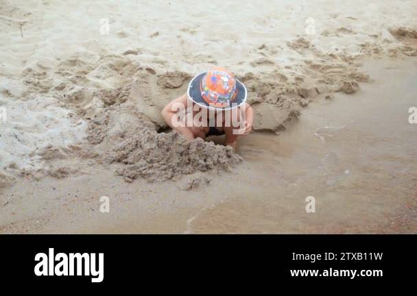 little boy digging a hole on the beach near the sea shore Stock Video ...