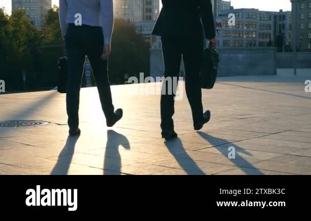Two businessmen with briefcases walking in city street with sun flare ...
