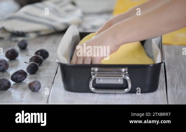 Woman puts yeast dough in a baking dish. Process of making plum cake ...