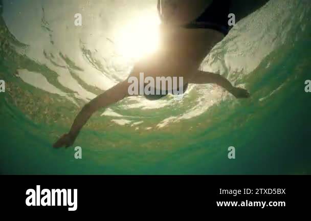 Following a woman swimming in pool, underwater view with sunset sun ...
