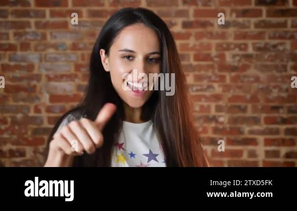 Young cute girl laughs and shows a like sign, smiling, brick wall in ...
