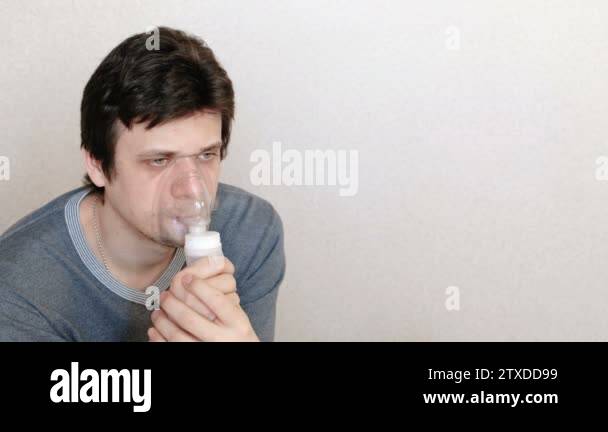 Use nebulizer and inhaler for the treatment. Young man inhaling through ...