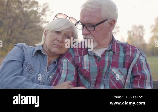 Close-up of a Caucasian senior couple sitting on the bench and talking. Mature husband calming ...