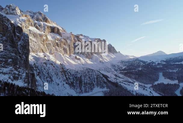 Going down aerial along snowy alpine steep rocky cliff valley with ...