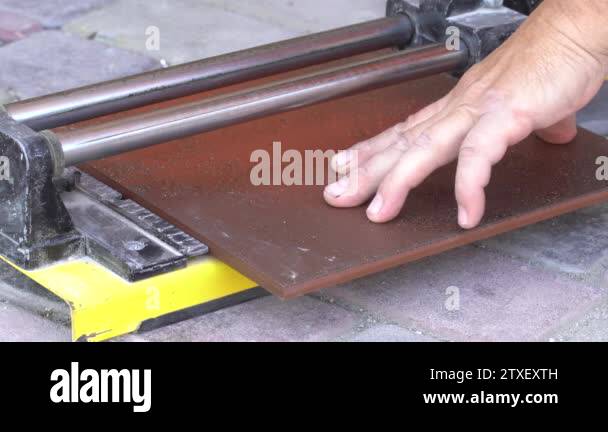 Tiler with a hand-held tile cutter cuts the tile on the floor, person ...
