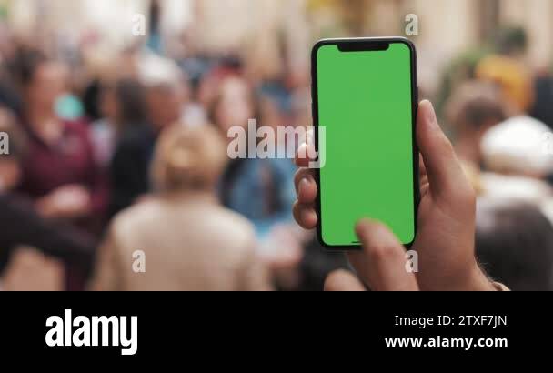 Closeup of a mans hand holding and using green screen mobile gadget with a vertical green screen ...
