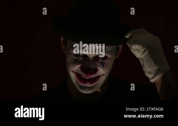 Terrible man in a clown makeup takes off his hat by welcoming his ...