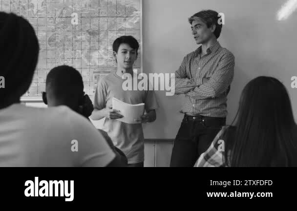 Teacher and teenage boy explaining lesson to positive pupils in a multi ...