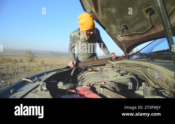 The blonde in the cap looks under the hood of the car is looking for a ...