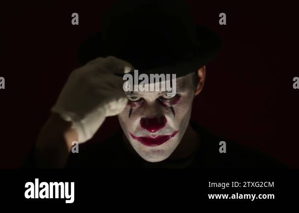 Terrible man in a clown makeup takes off his hat by welcoming his ...