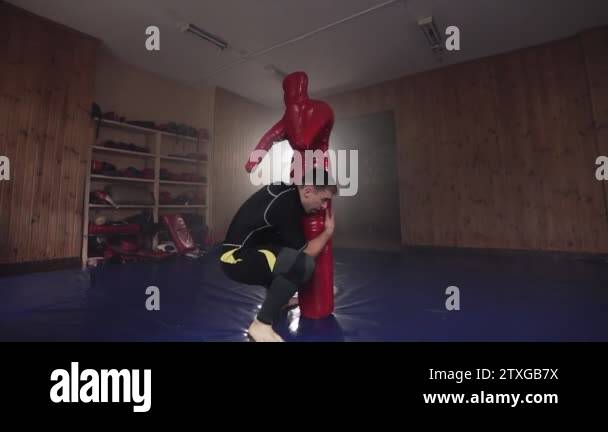 Young man hitting dummy punching bag in gym during practicing combat ...