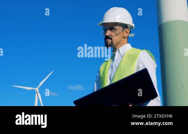 Male energetics worker is standing with his laptop near a wind turbine ...