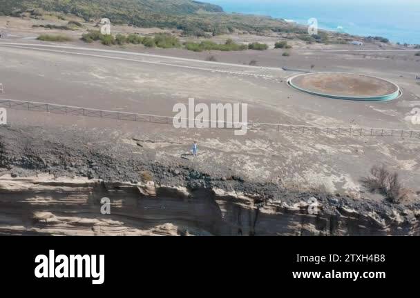 Woman walks along the edge of precipice towards an old lighthouse ...