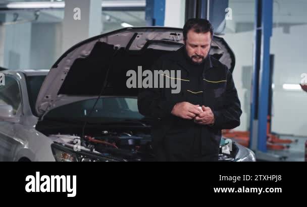 Old man mechanic in a stylish uniform wearing wireless headphones ...