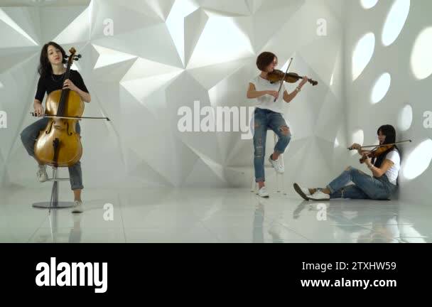Two girls playing the violins one on the cello in the white studio ...