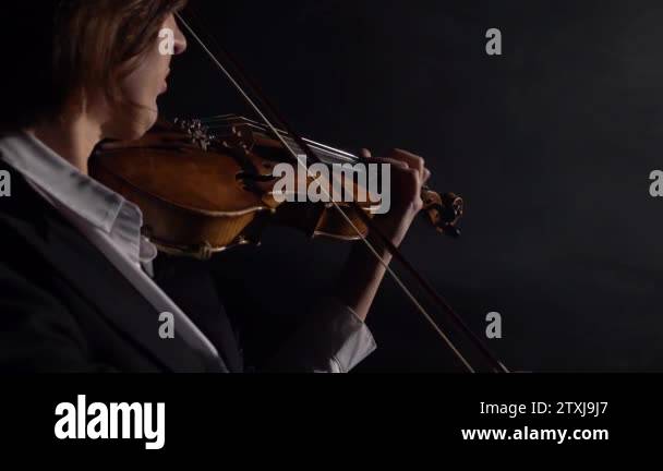 Dark studio where a musician plays the violin while standing with his ...