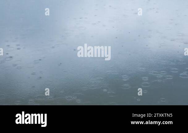 Rain drops fall on water surface of pond, lake or river forming a ...