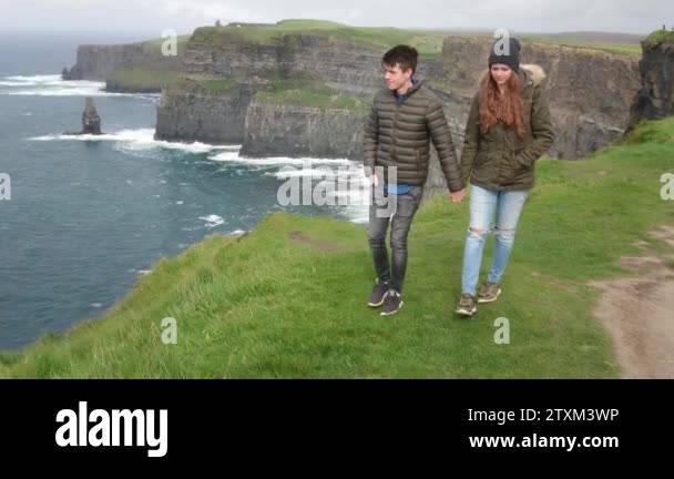 Young couple walks hand in hand on the edge of the famous Cliffs of Moher Stock Video Footage ...