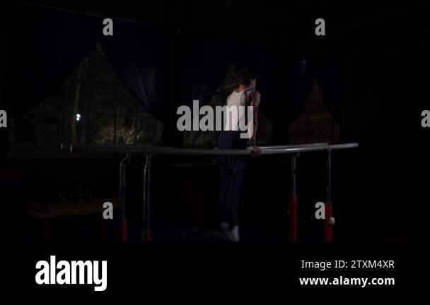Male gymnast acrobat performs handstand on parallel bars in a dark room ...
