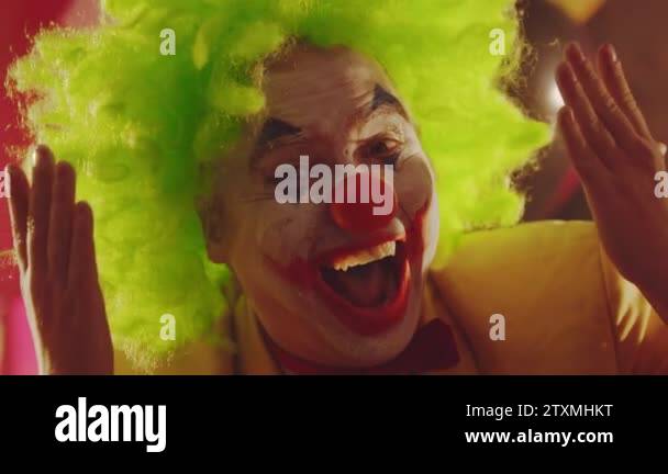 A crazy smiling clown closing his face with his hands and performing ...