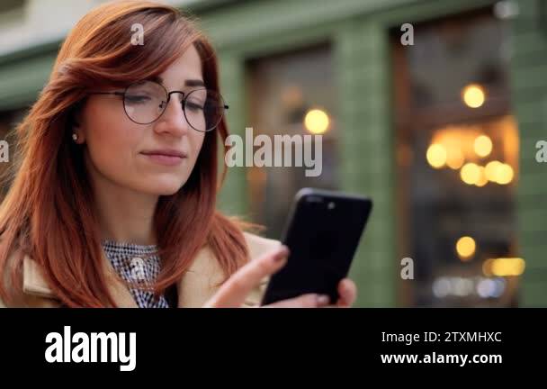 Beautiful young woman in stylish coat using smart phone app in the city street, professional ...