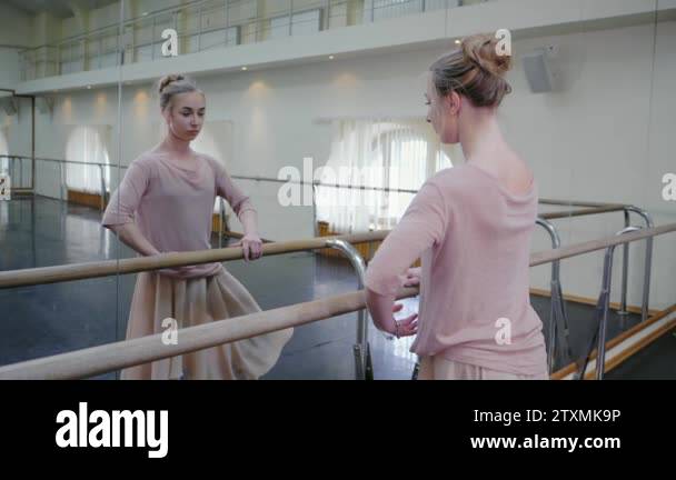 Ballerina in beige sweatsuit and pointe stretches on barre in ballet ...