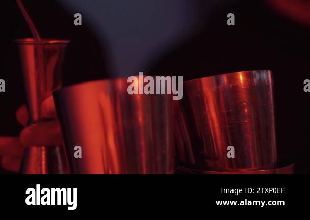 Waiter wearing black is preparing soft drink in bar shaker at night ...