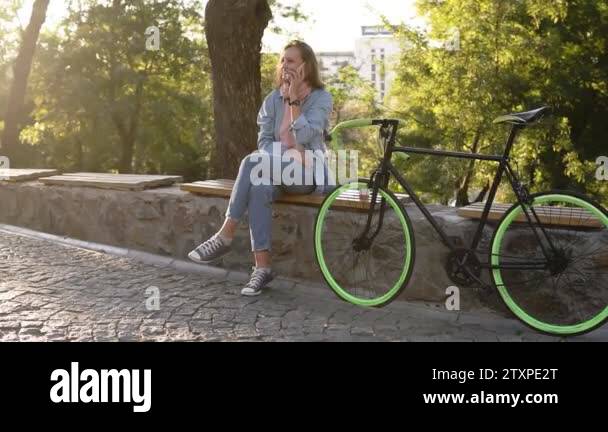 Fair haired girl sitting on the bench or parapet in the city park with ...