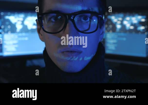 Portrait of Hacker programmer in glasses looks at camera while blue ...