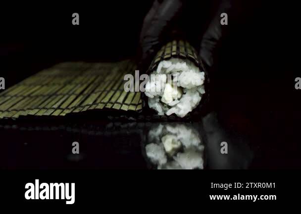 Sushi rolling process with black bamboo makisu, isolated on black ...