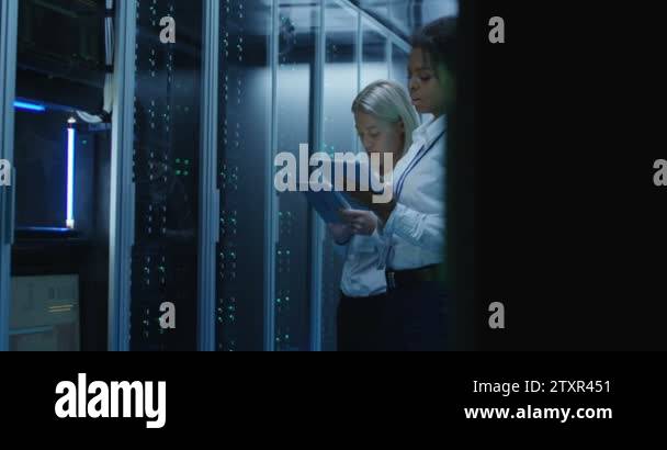 Two women are working in a data center with rows of server racks Stock ...