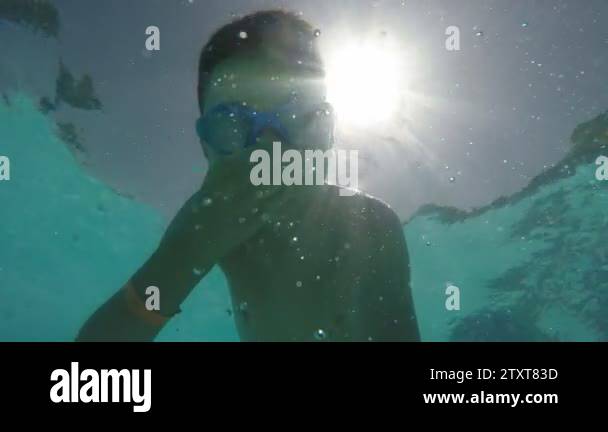 Small boy looking around underwater with a shining sun behind in slow ...
