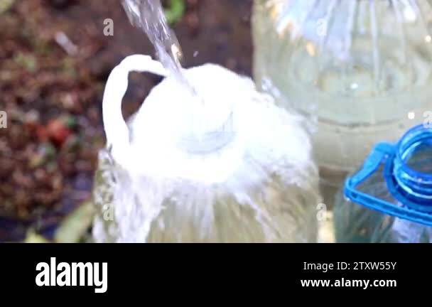 filling plastic bottles with clean drinking water from a rubber hose ...