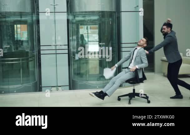 Slow motion of happy guys in suits having fun in office lobby riding ...