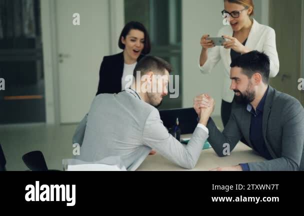 Male office workers are having fun doing arm-wrestling while girls are ...