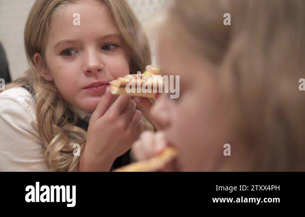 A close up of two girls eating pizza. The image to the left is blurred ...