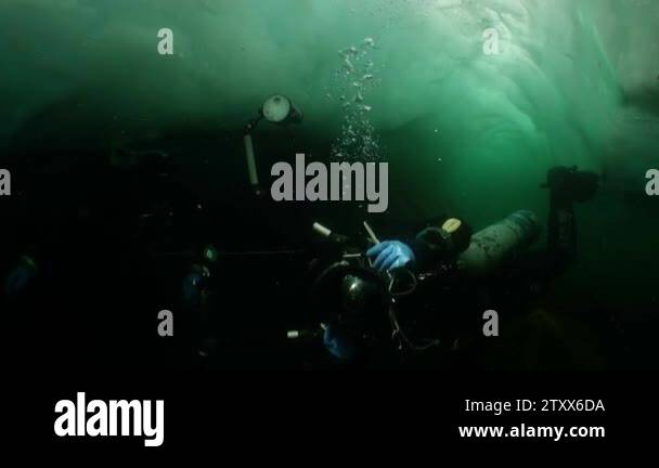 Underwater cameraman with camera and technical diver under ice of lake ...