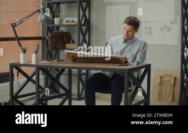 Architect man sits at drafting table in modern industrial office during ...