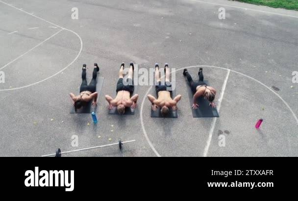 two women with two men doing push ups and jumping at stadium, burpee ...
