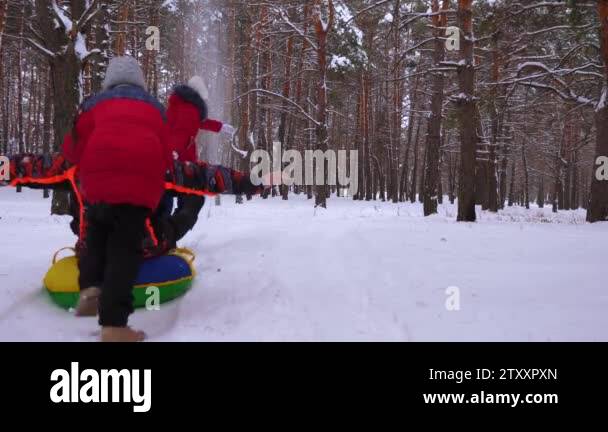 children ride daddy on sled and an inflatable snow tube. Happy family ...