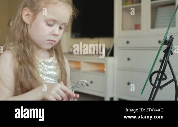 little girl with red hair tries to curl her eyelashes with forceps ...