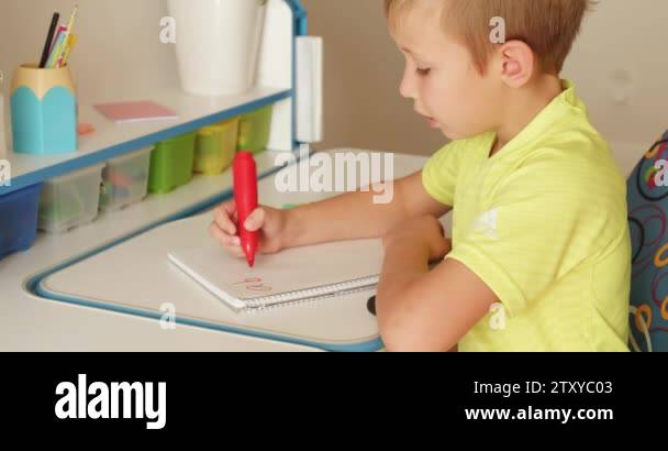 Child writes the characters in school notebook. Schoolboy is doing ...