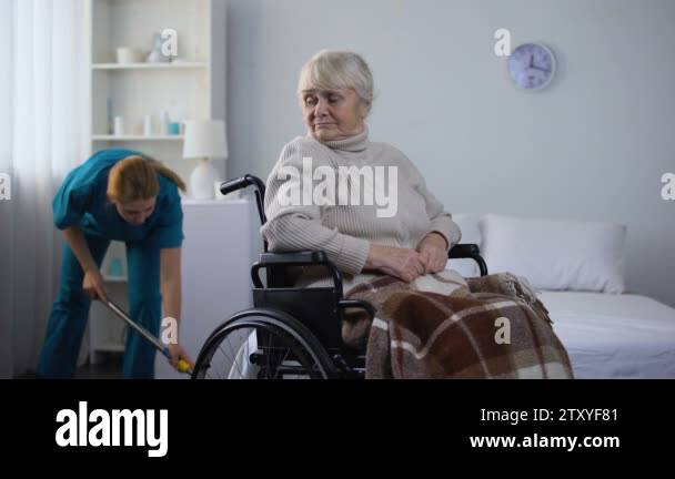 Sad woman in wheelchair watching hospital janitor cleaning room ...