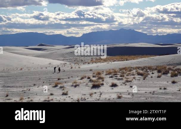 People walk on white gypsum sands in a desert landscape against a ...