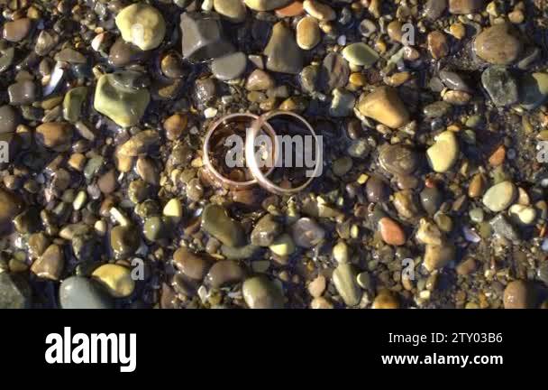 Two gold wedding rings lying on beach stones shining on sun light close ...