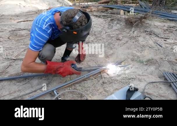Welding of iron fittings. A welder squatting welds rods. The electrode ...