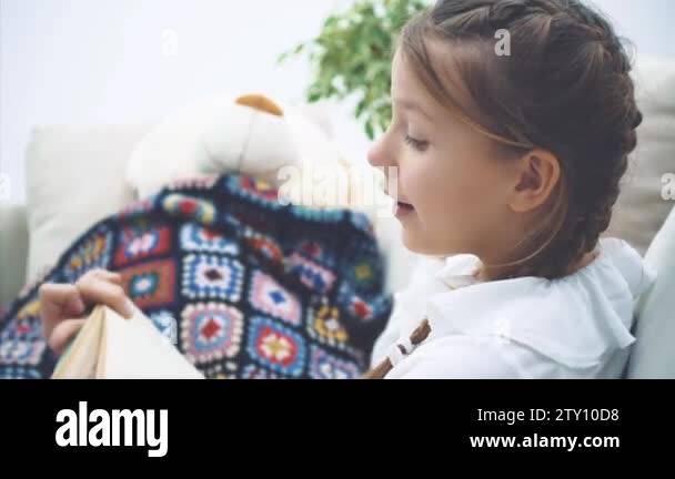 Cute little girl sitting with her legs curled up, reading fairy-tale ...