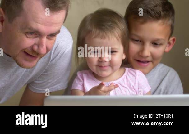 Parent and two children look at laptop screen having fun together at ...